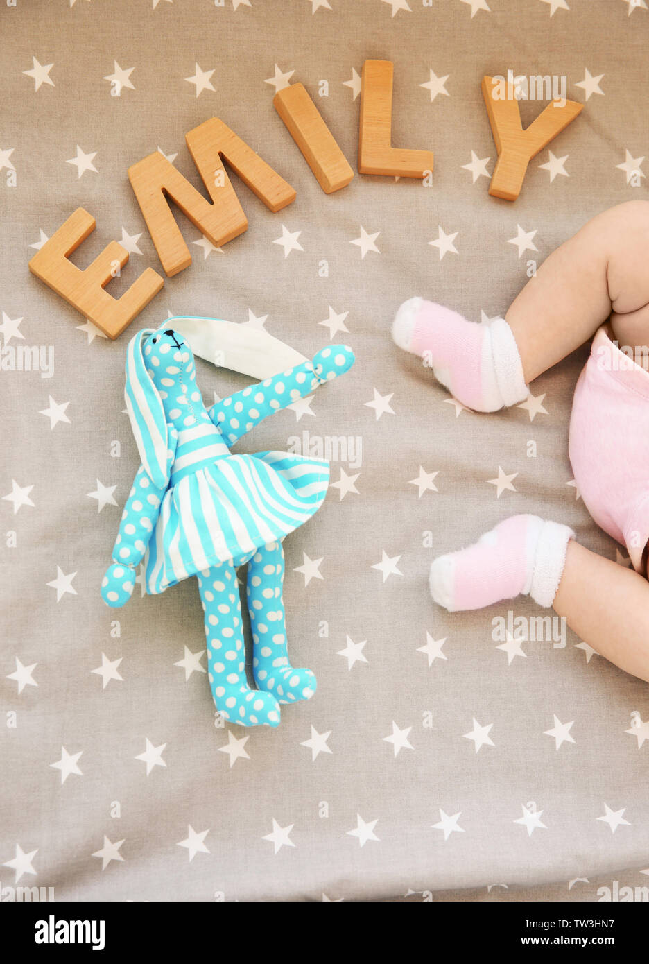 Legs of cute baby, toy and word EMILY composed of wooden letters on bed ...