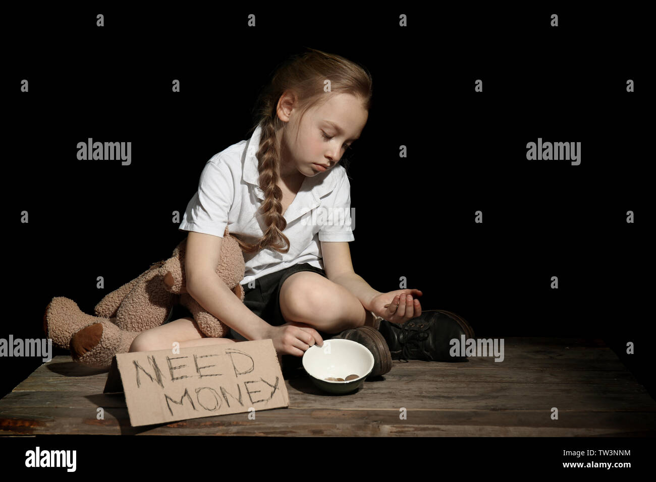 Poor little girl with bowl and piece of cardboard on black background ...
