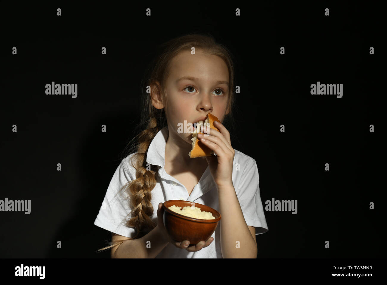 Poor little girl eating bread on black background Stock Photo - Alamy