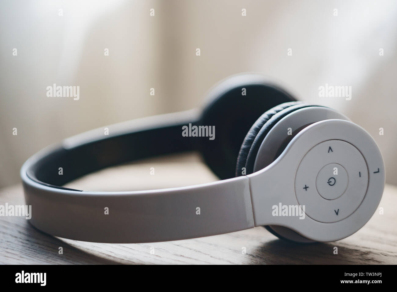 White wireless headphones placed on natural wooden surface on a blurred ...