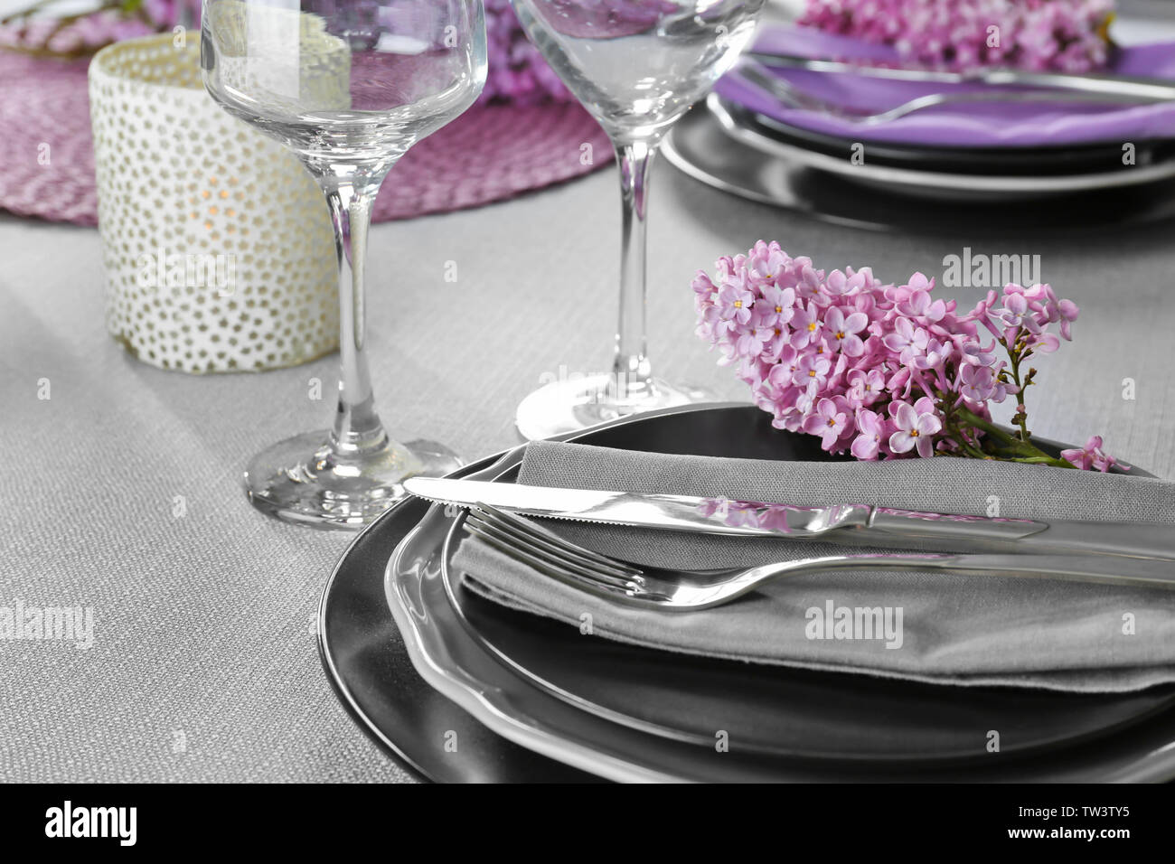 Beautiful table setting with silver cutlery and lilac as floral decor ...
