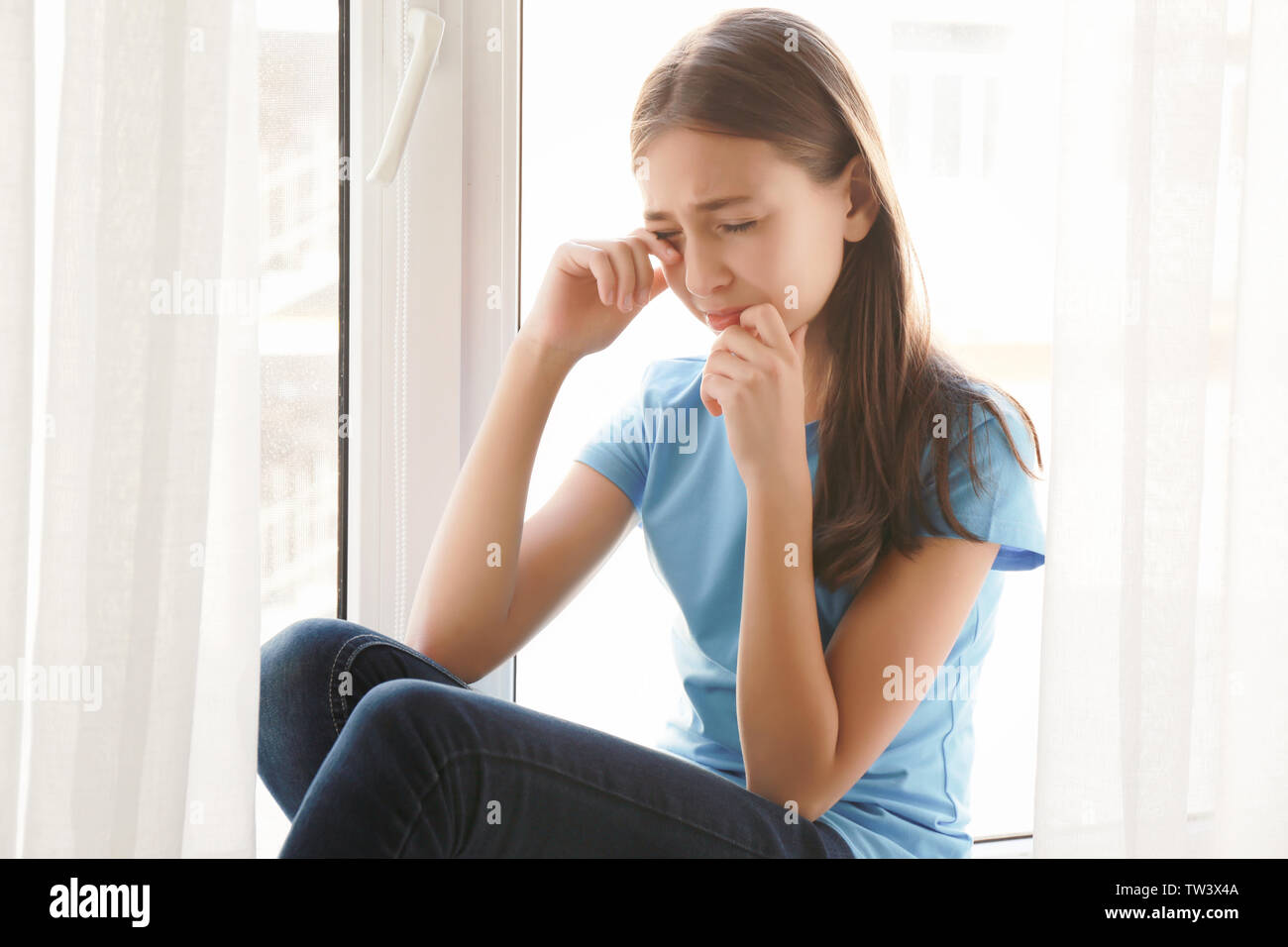 Cute sad girl sitting on window sill at home Stock Photo - Alamy