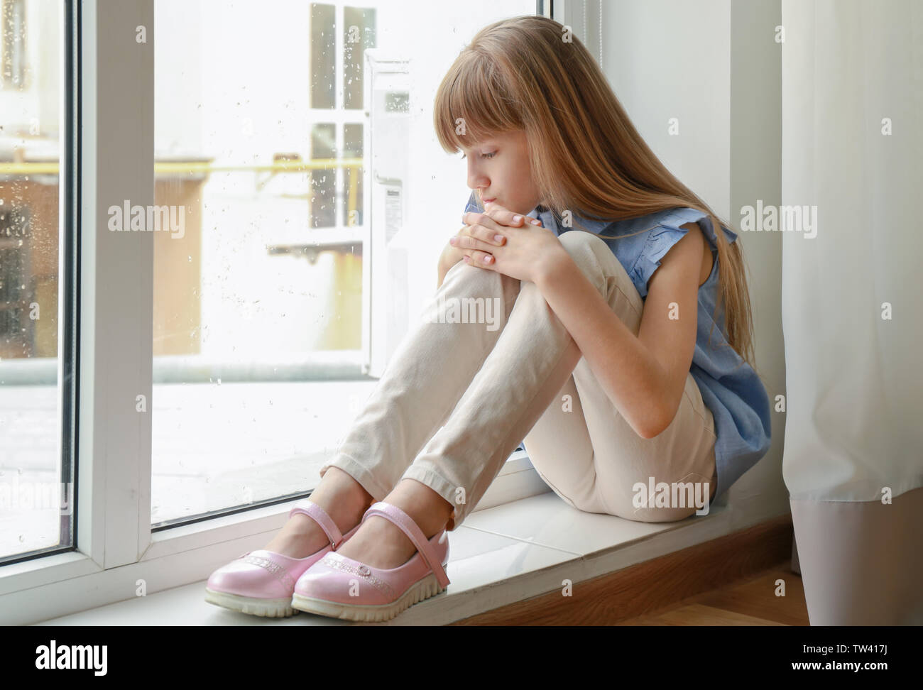 Sad little girl sitting on window sill at home Stock Photo - Alamy