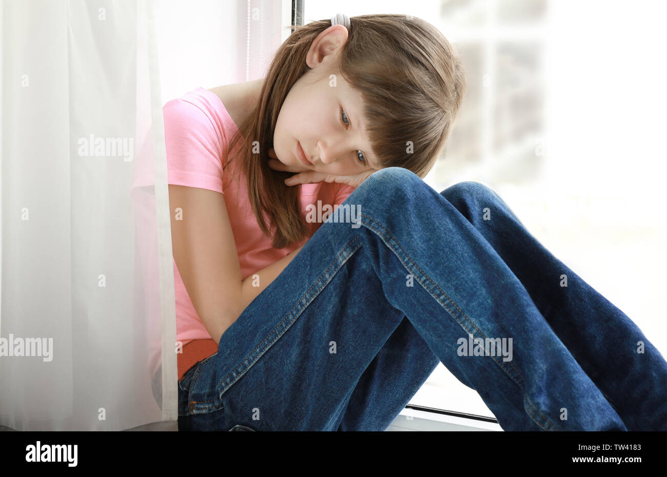 Sad little girl sitting on window sill at home Stock Photo - Alamy