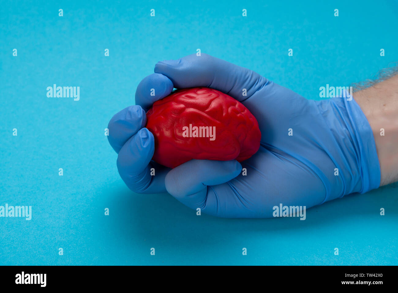 A latex glove hand squeezes a red brain. Brain treatment Stock Photo ...
