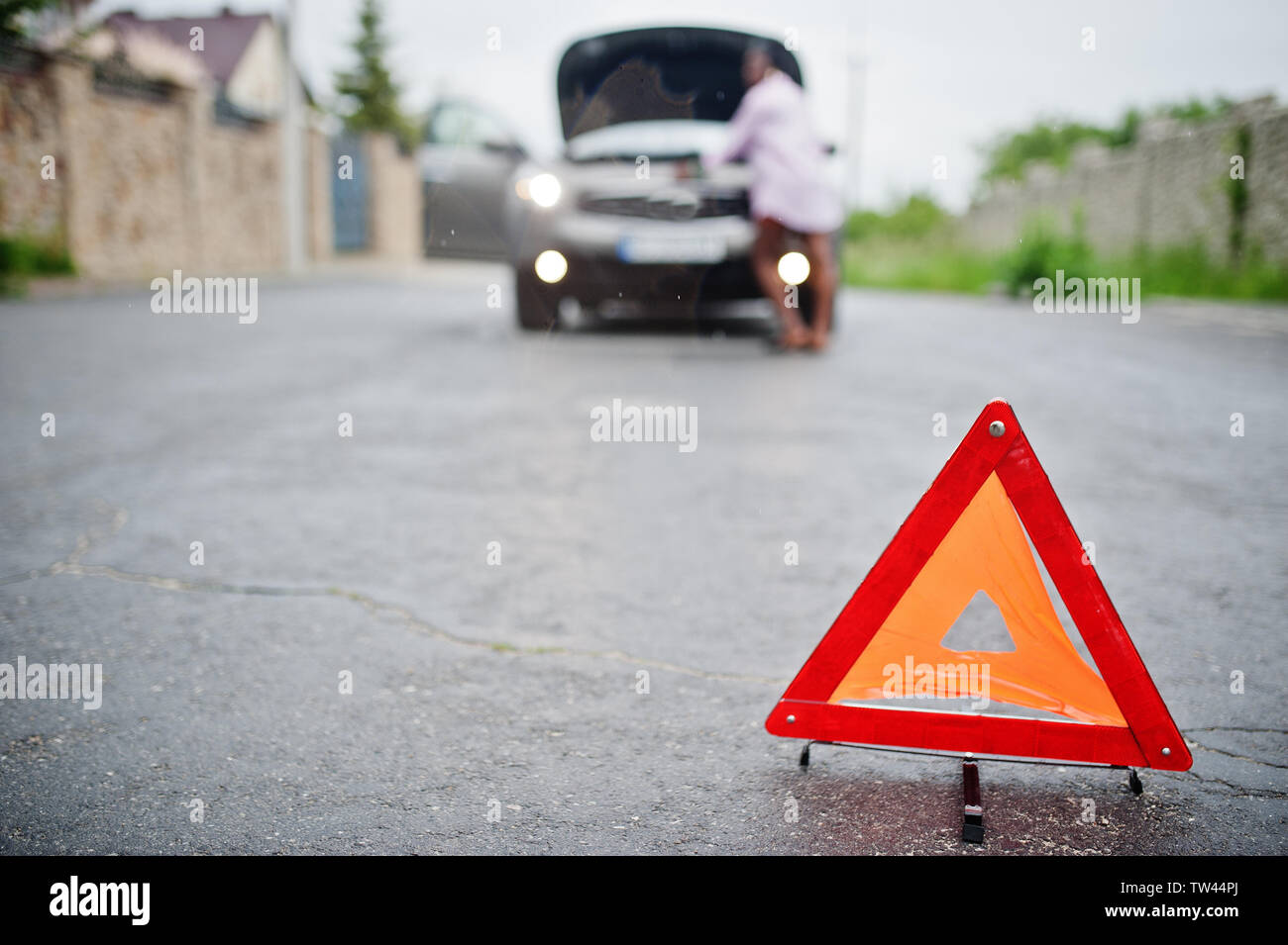 Young sad african woman stand with emergency triangle against car with ...