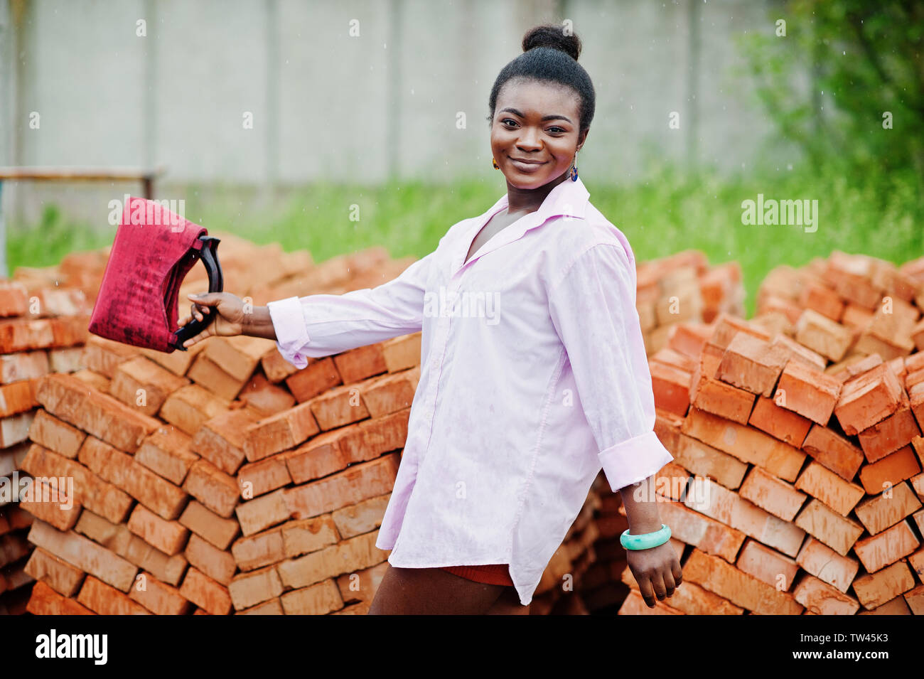 African woman in pink large shirt posed against bricks Stock Photo - Alamy