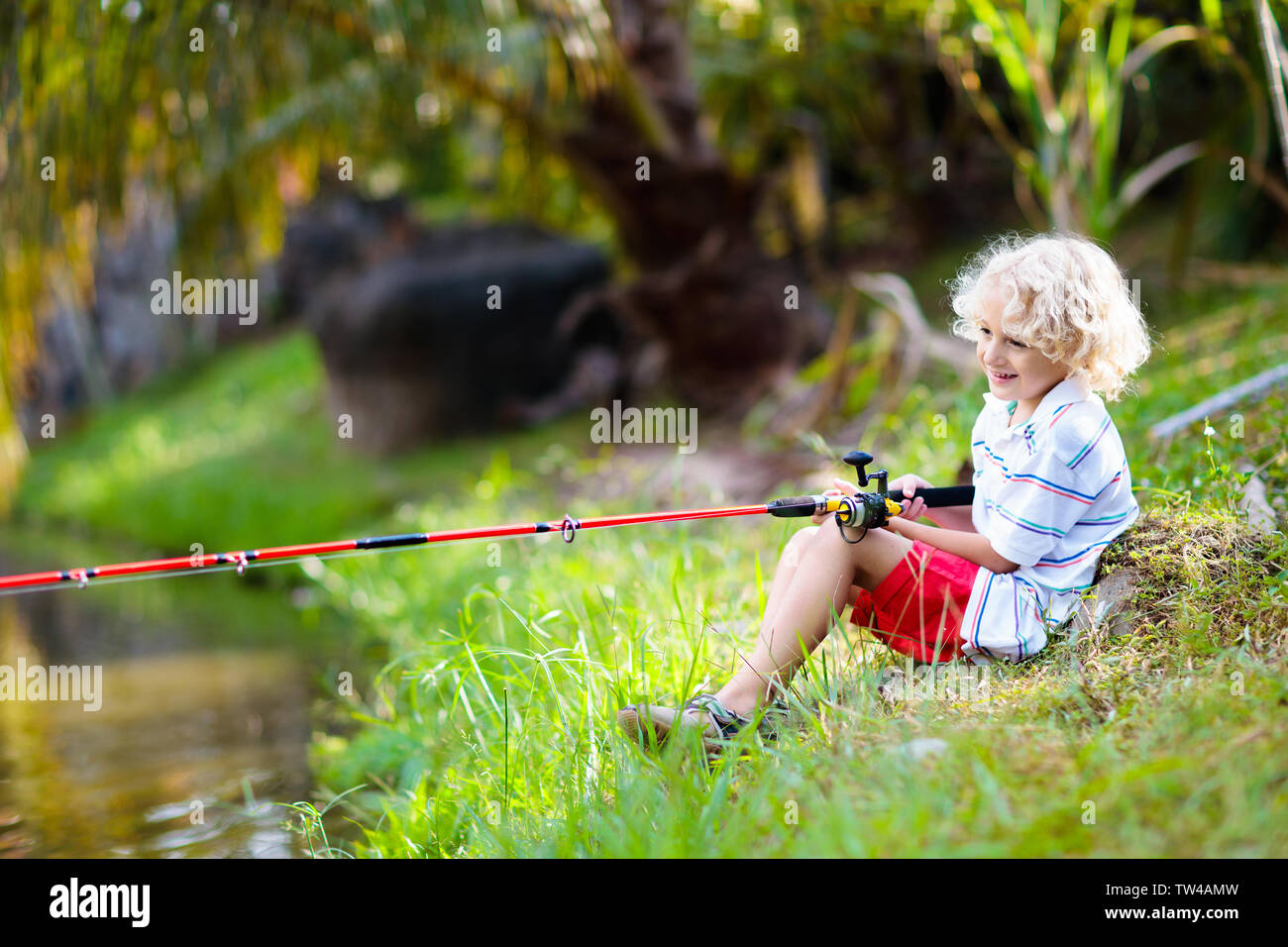 Boy fishing. Child with red rod catching fish in river on sunny summer ...