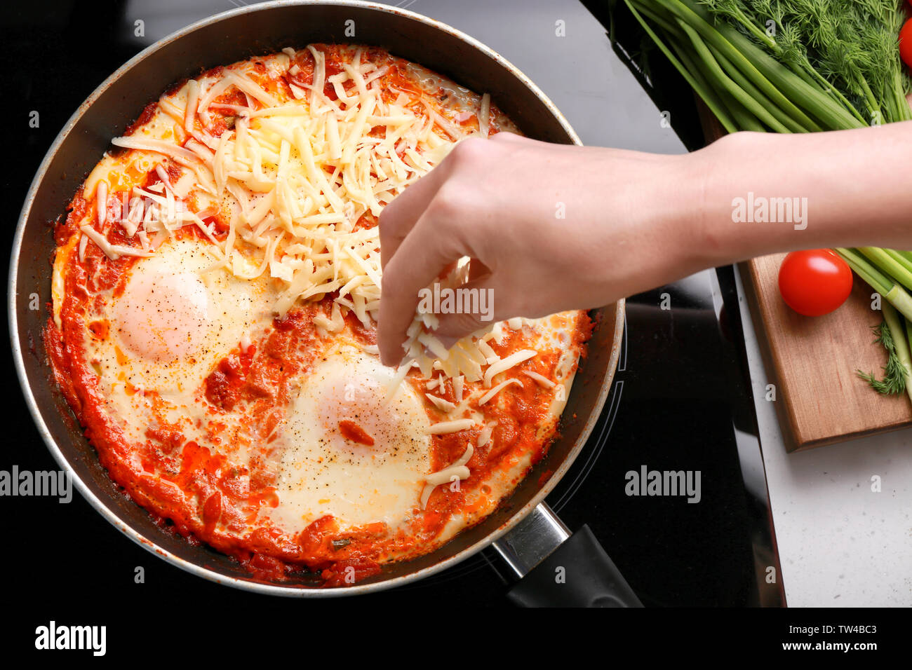Woman pouring cheese on eggs in purgatory Stock Photo - Alamy
