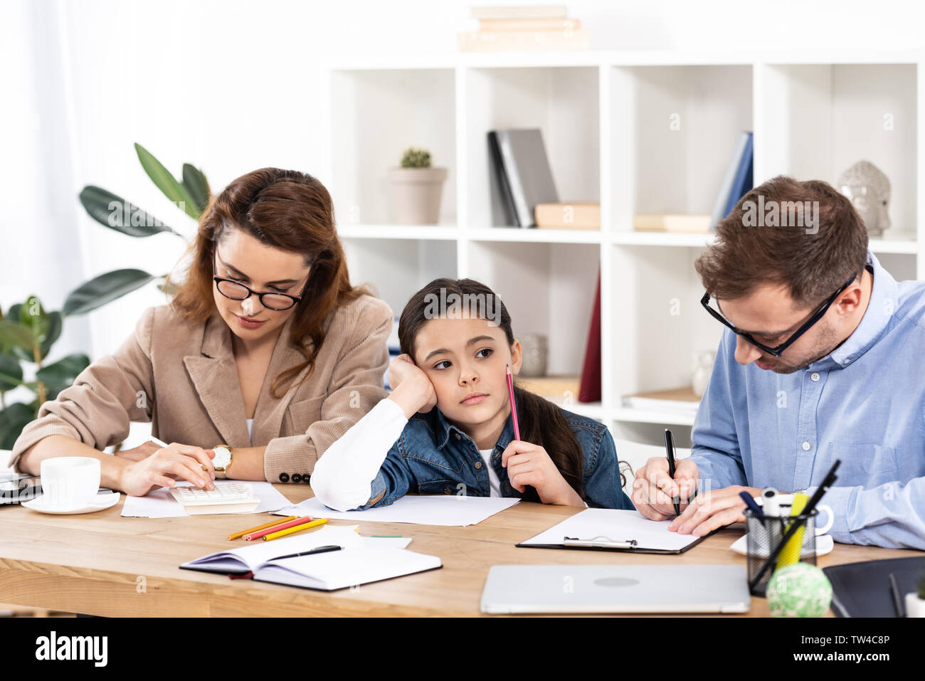 sad child holding pencil near parents in glasses working in office ...