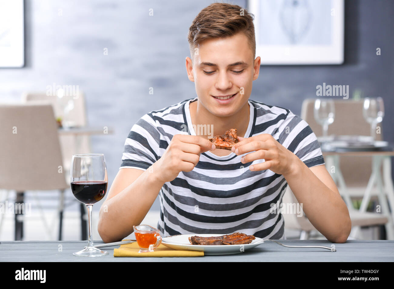 Young man eating delicious ribs in restaurant Stock Photo - Alamy
