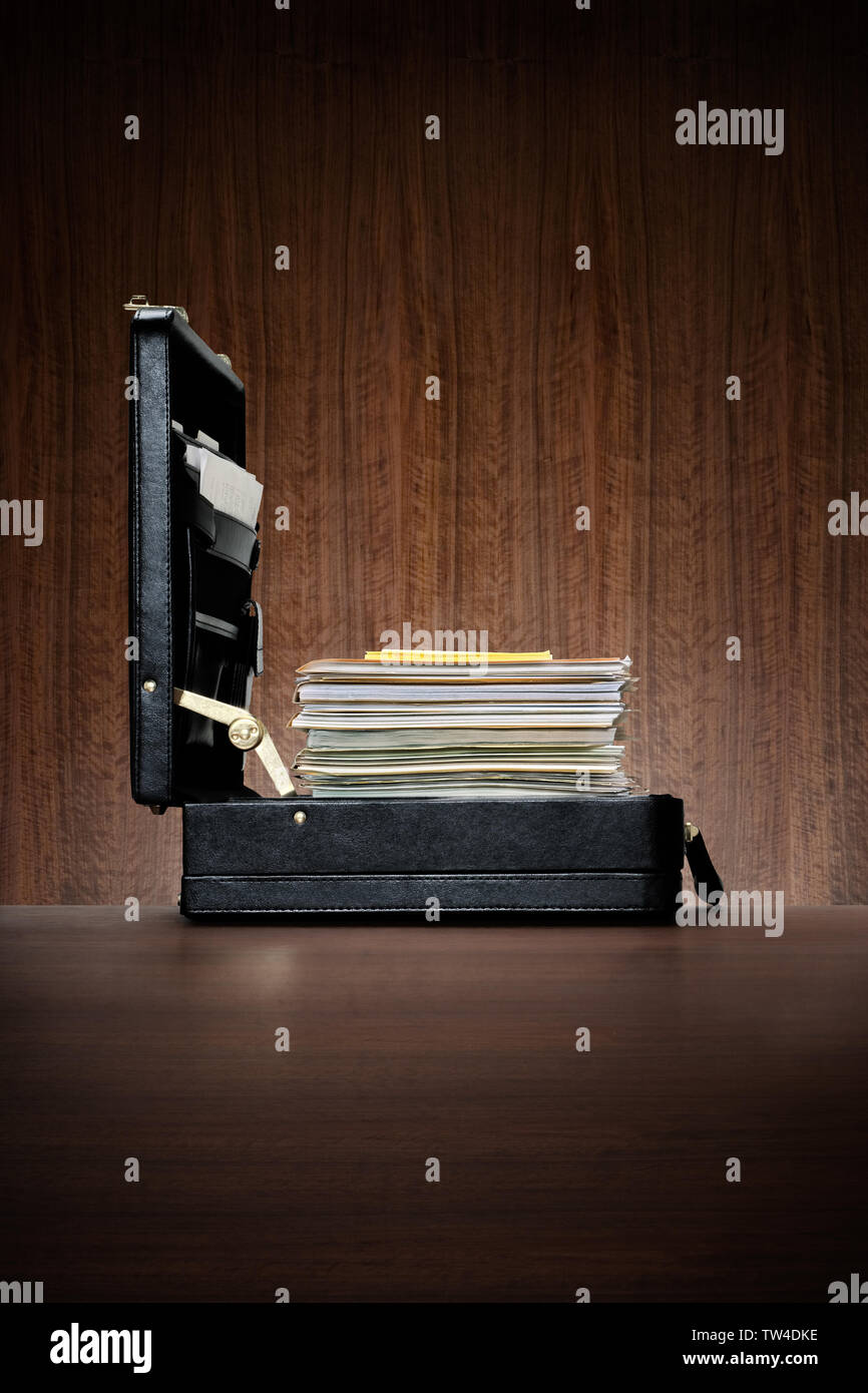 Black leather attache case with tall stack of files and folders on dark ...