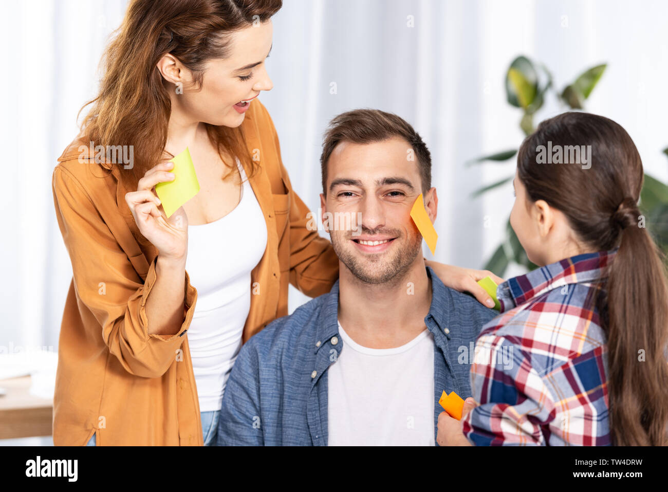 cheerful woman and cute kid putting yellow sticky notes on happy man ...