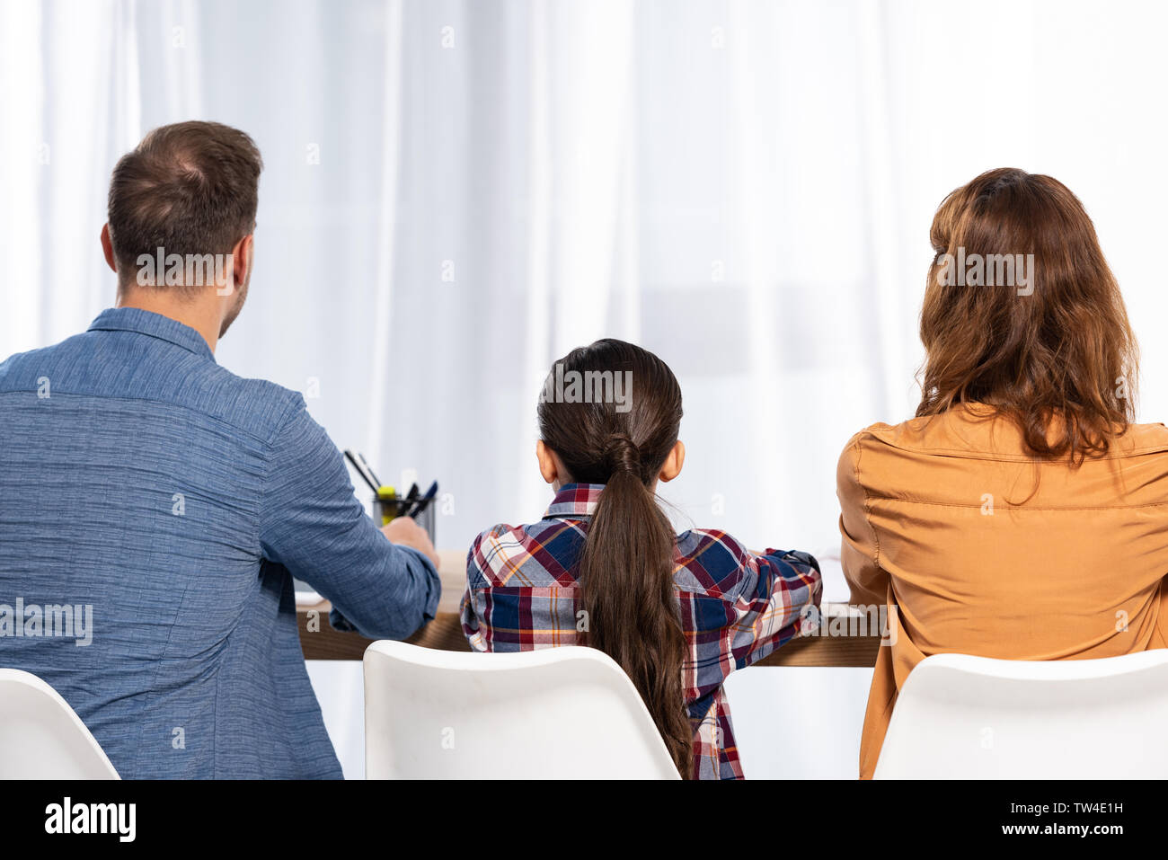 back view of parents sitting near daughter on chairs Stock Photo - Alamy