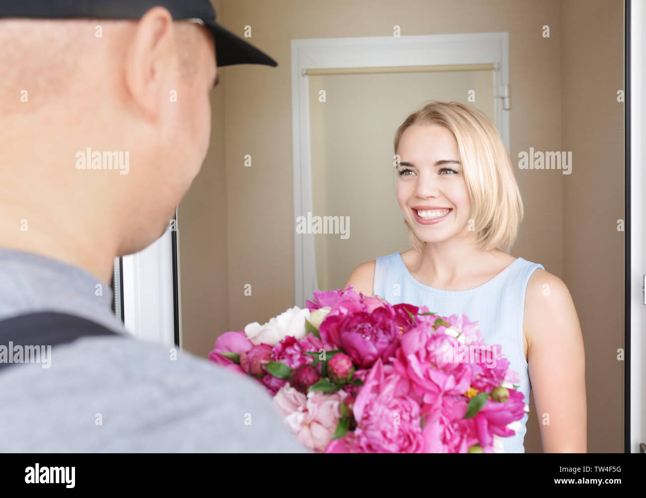 Young woman receiving beautiful peony flowers from delivery man Stock ...