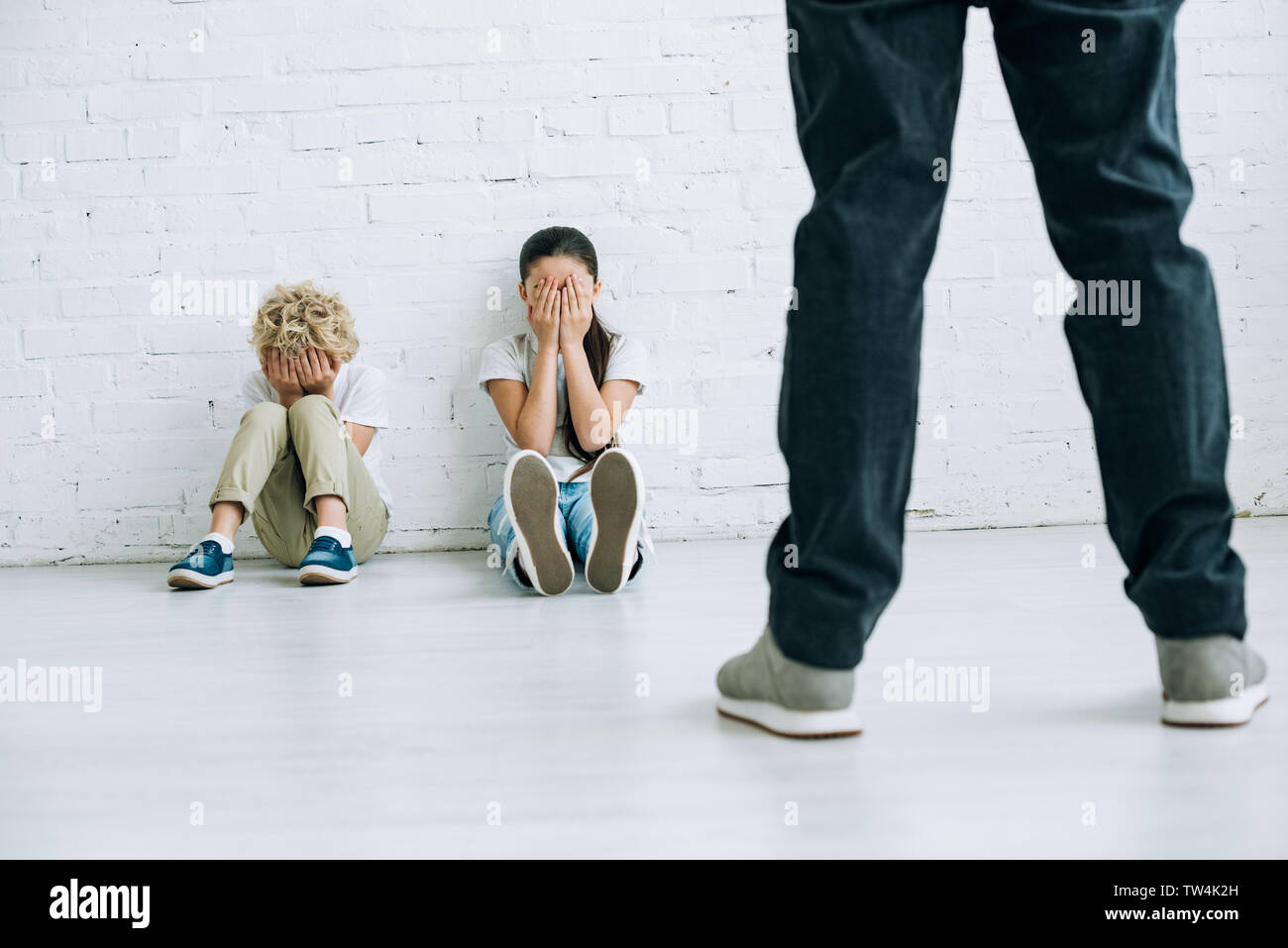 cropped view of abusive father holding belt and scared kids sitting on ...