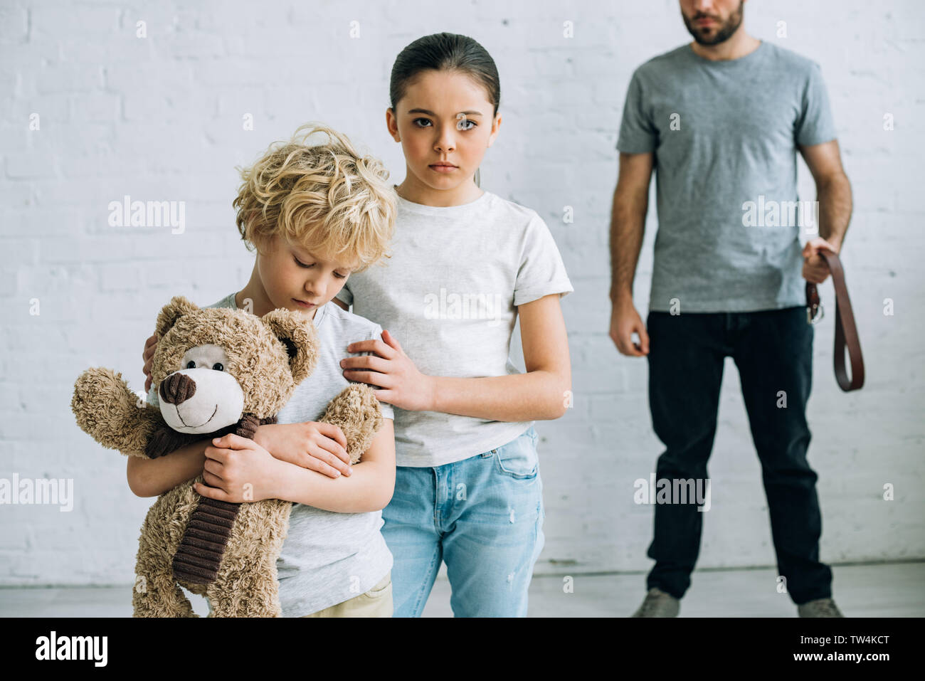 partial view of abusive father with belt and sad kids with teddy bear ...