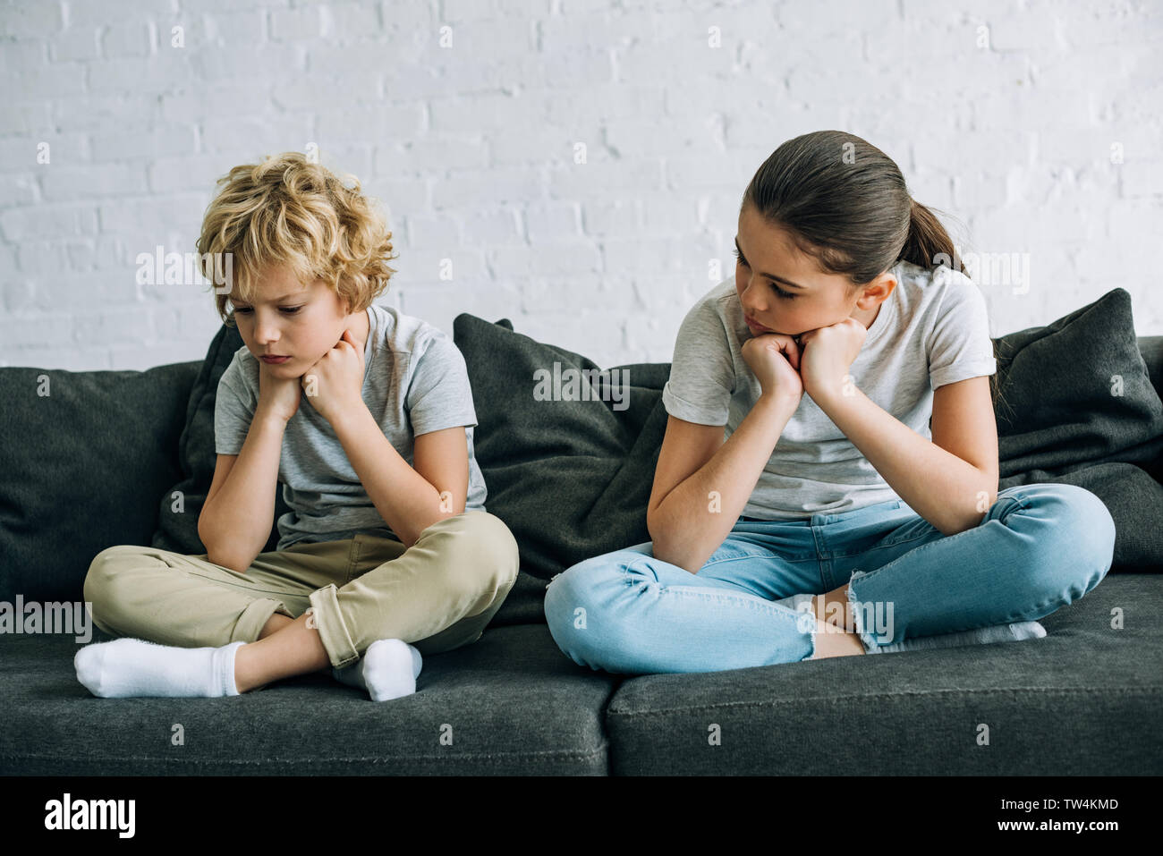 two sad kids sitting on sofa in living room Stock Photo - Alamy