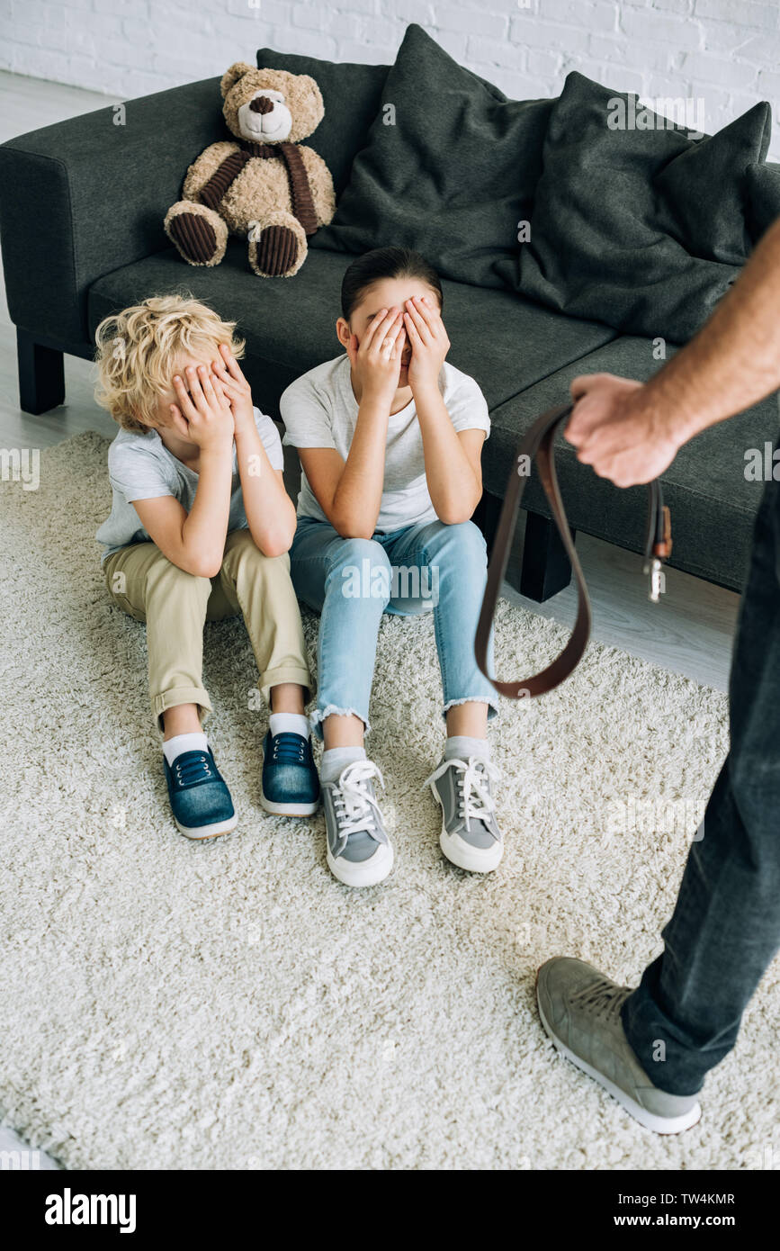 partial view of father with belt and upset kids sitting on floor Stock ...