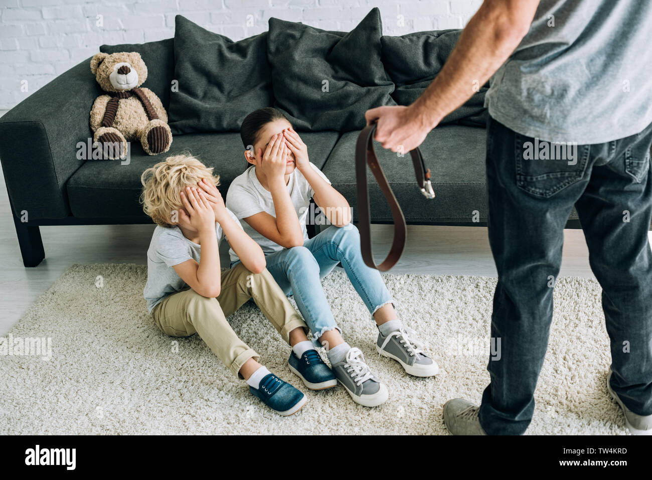 partial view of father with belt and upset kids sitting on floor Stock ...