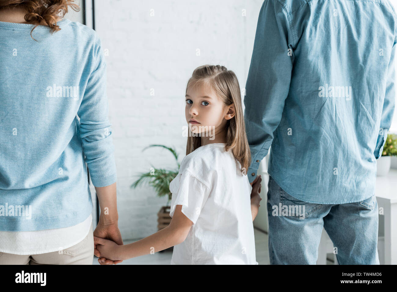 sad kid standing with parents and holding hands at home Stock Photo - Alamy