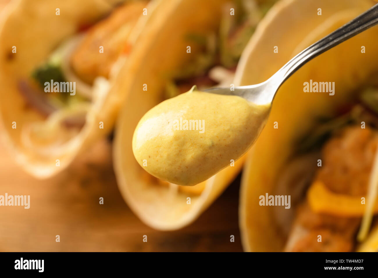 Spoon with tasty creamy sauce for fish taco on blurred background Stock ...