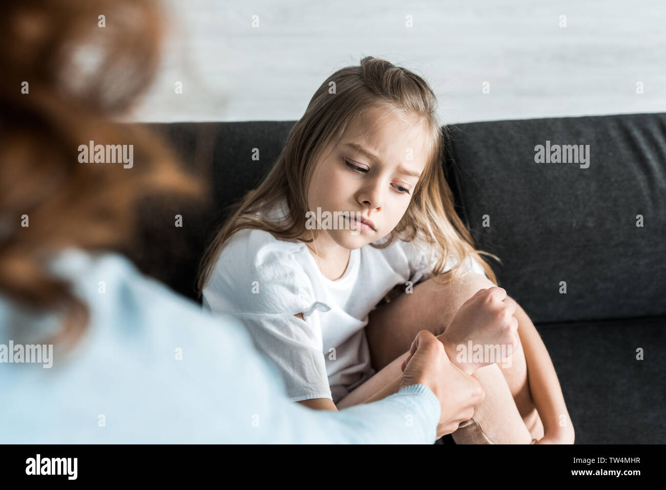 selective focus of scared kid sitting on sofa near mother holding hand ...