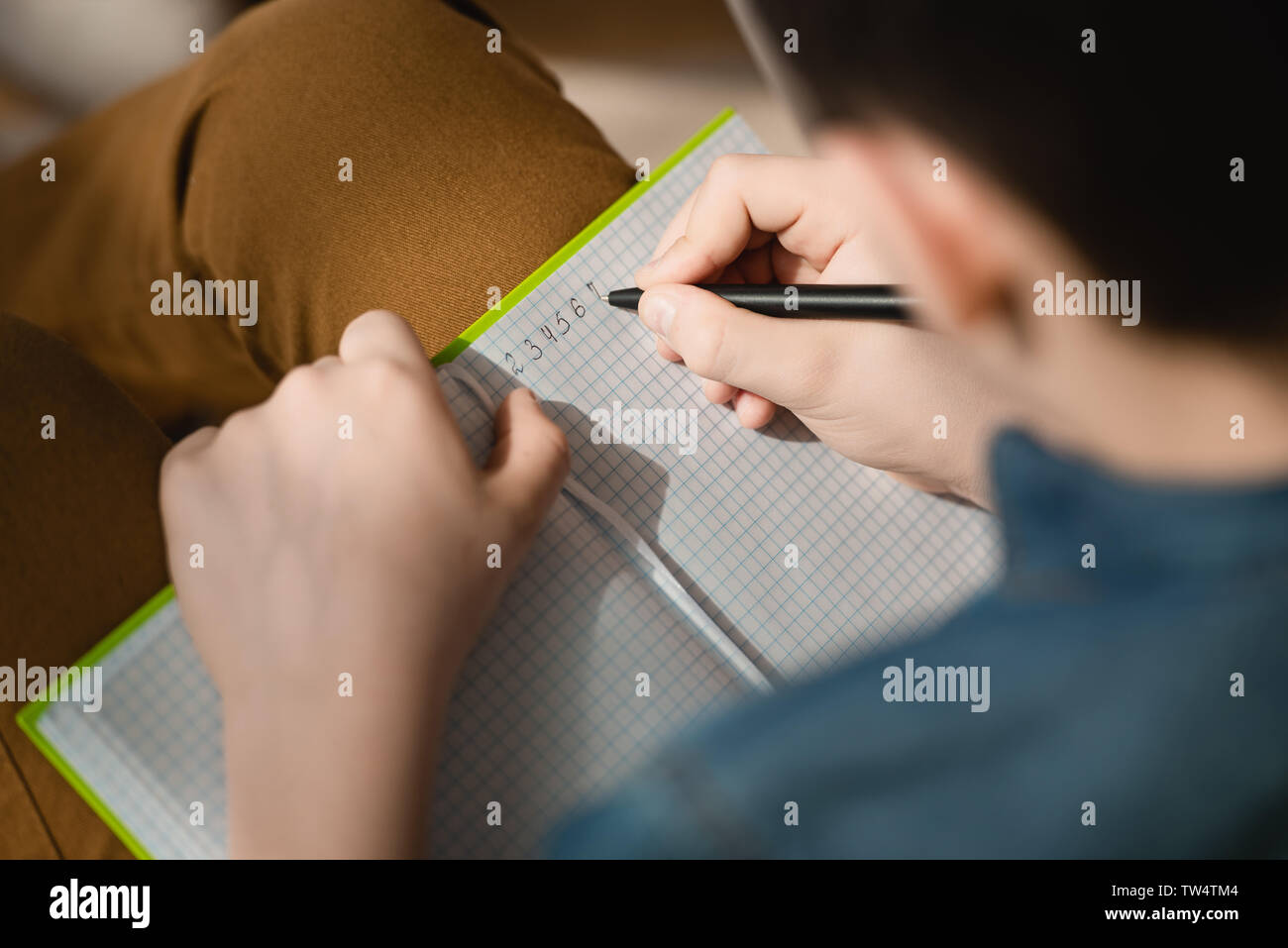 selective focus of schoolboy writing in copy book while making ...