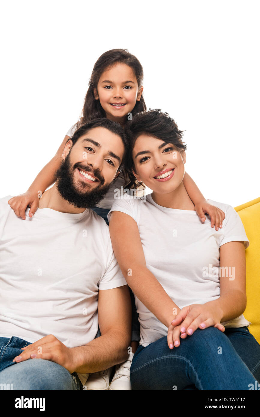 happy latin parents smiling while sitting on sofa near daughter ...