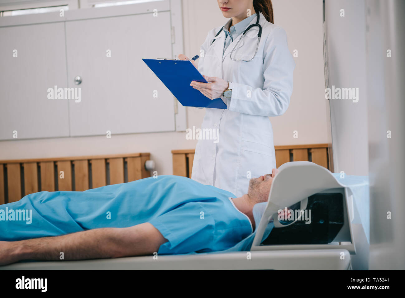 cropped view of young radiologist writing on clipboard while standing ...