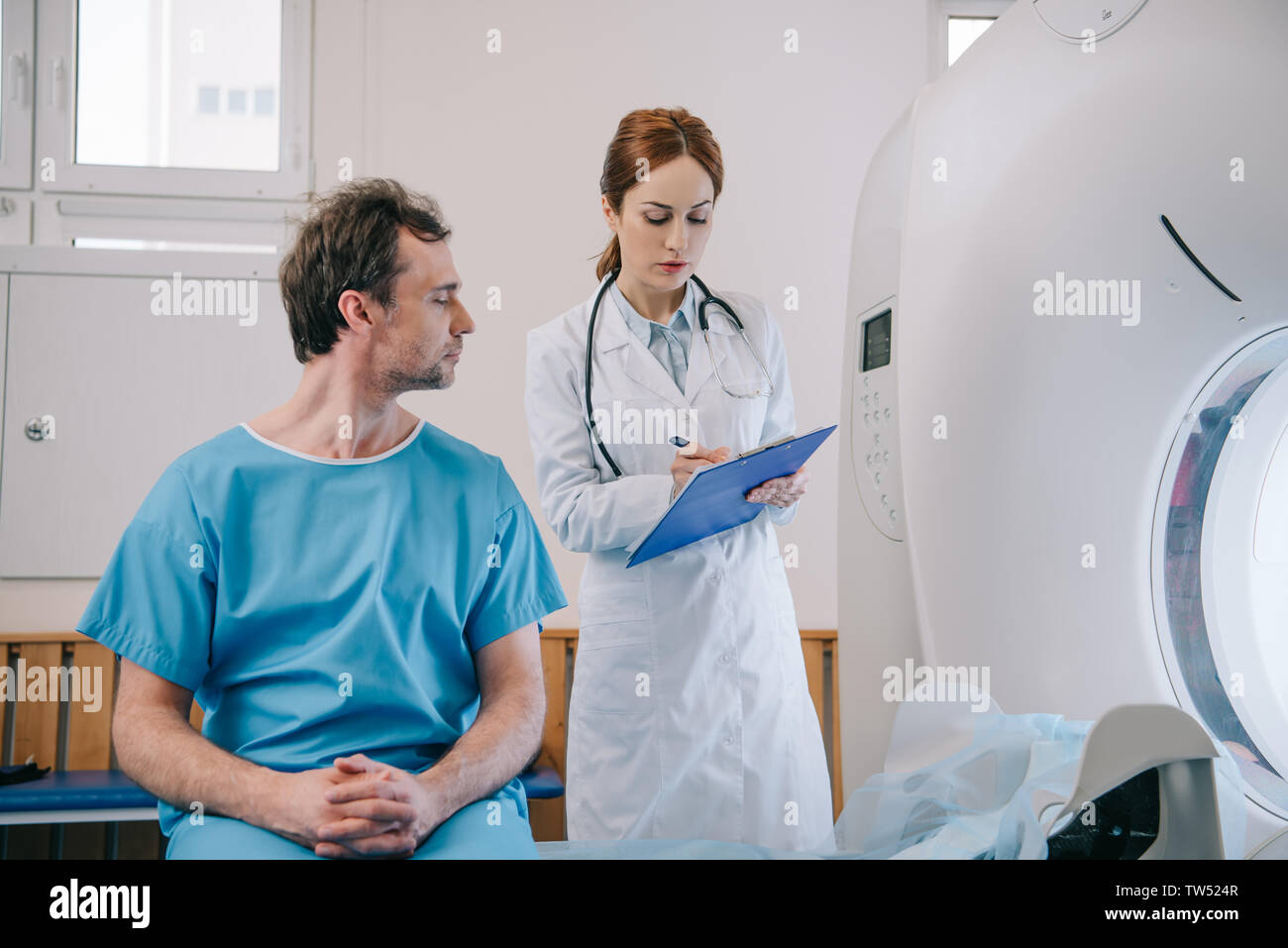 man sitting on ct scan bed near attentive radiologist writing on ...