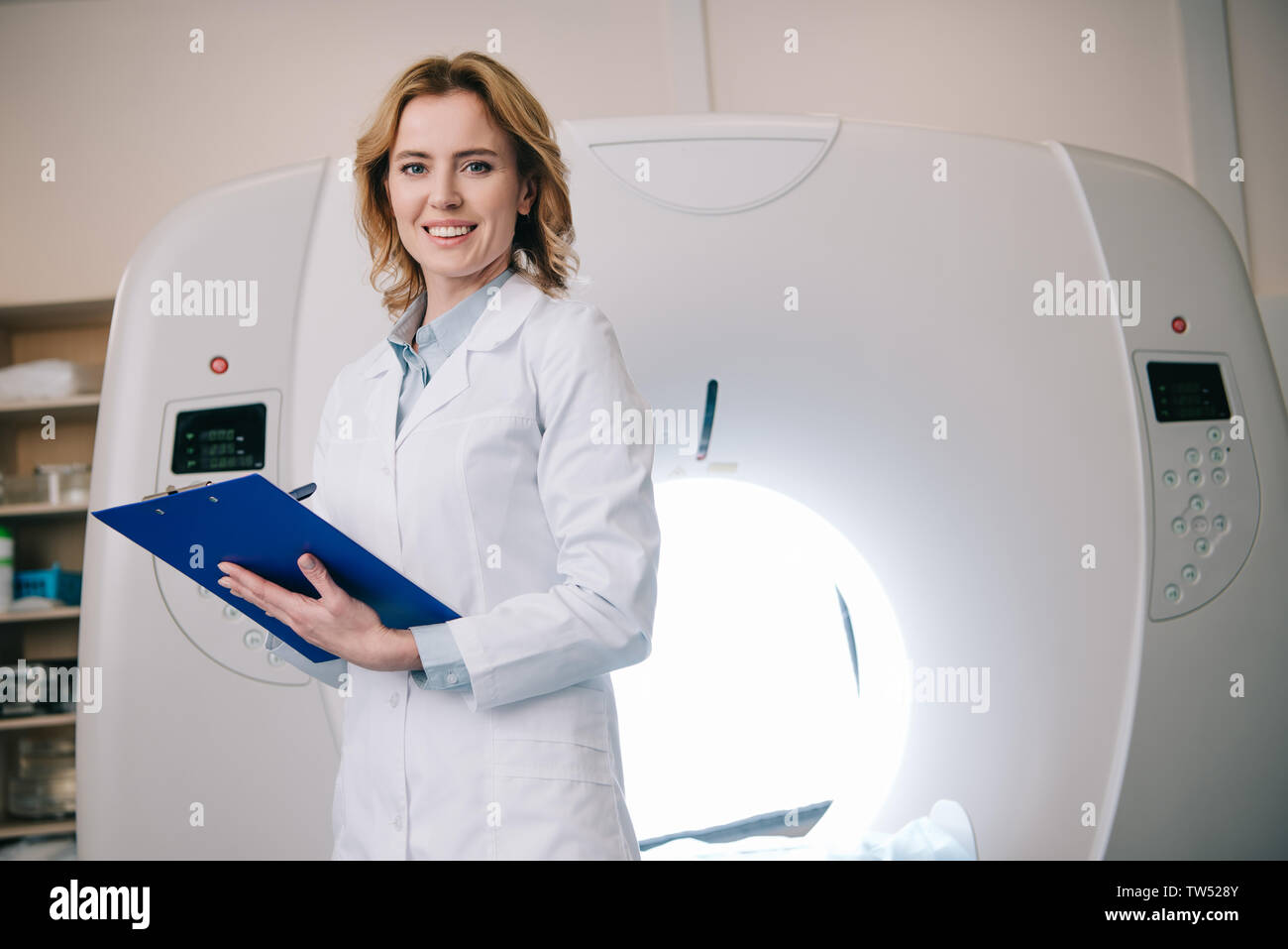 smiling radiologists writing on clipboard while standing near computed ...