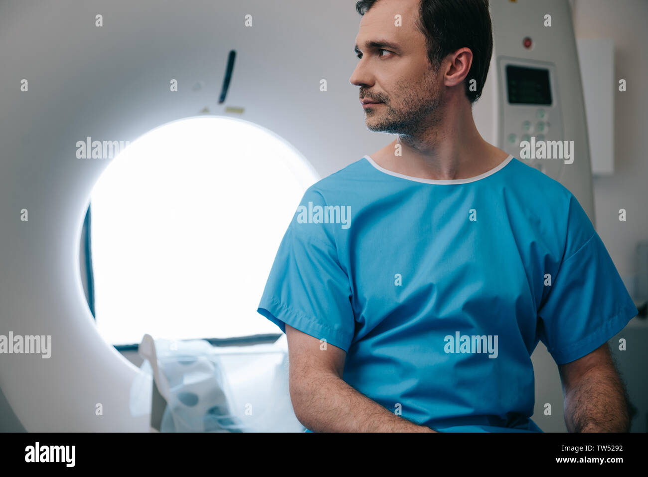 thoughtful patient sitting on ct scanner bed in hospital and looking ...