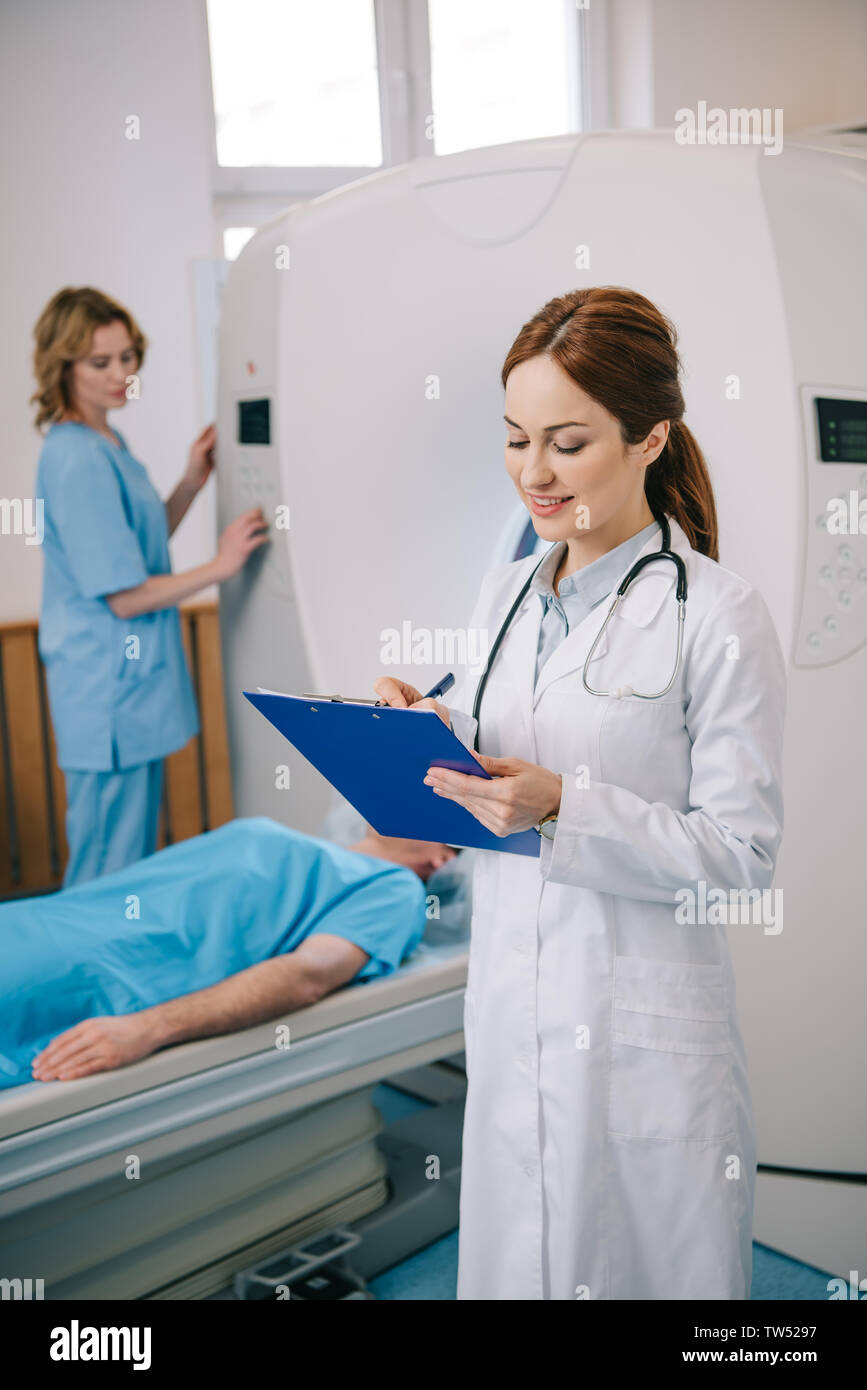 selective focus of radiologist writing on clipboard while assistant ...