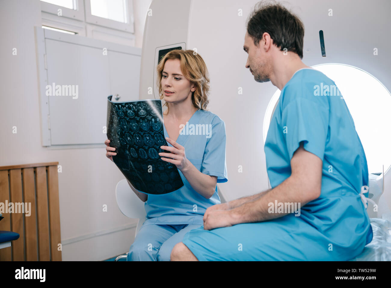 attentive radiographer looking at x-ray diagnosis near patient sitting ...