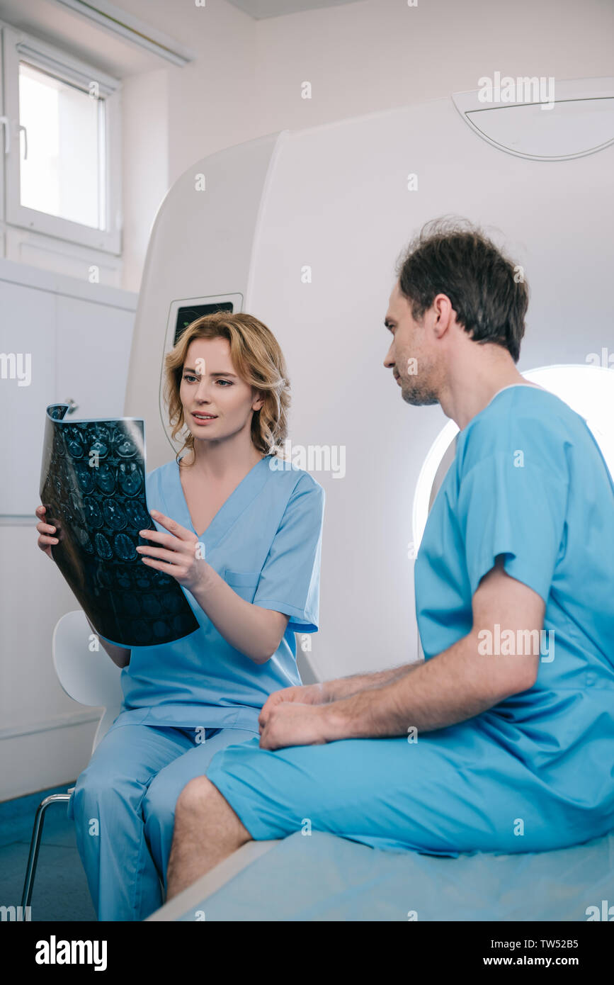 beautiful doctor looking at x-ray diagnosis near patient sitting on mri ...