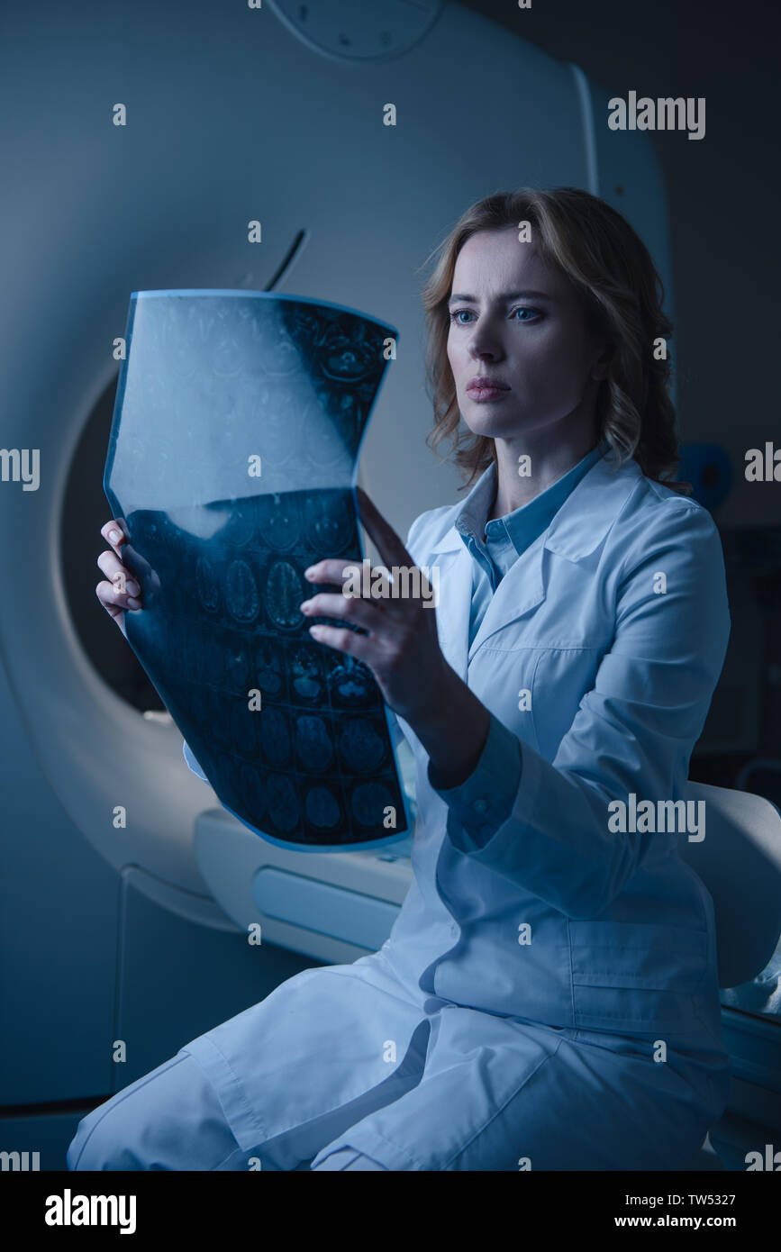 serious doctor looking at x-ray diagnosis while sitting near ct scanner ...