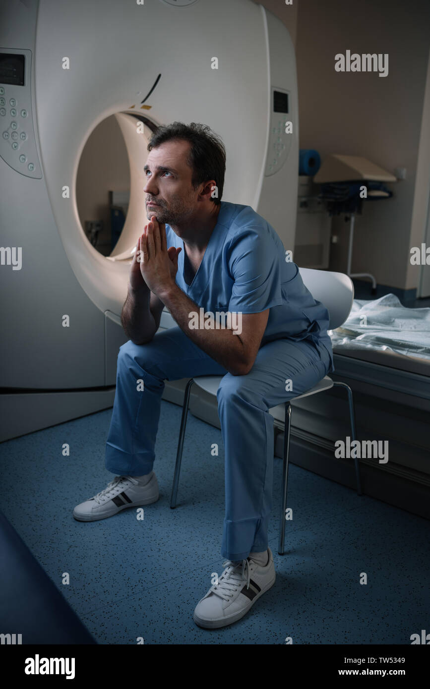 serious doctor sitting near computed tomography scanner in hospital and ...