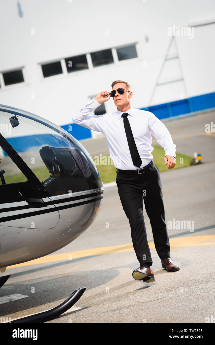 handsome Pilot in formal wear adjusting sunglasses and walking near ...