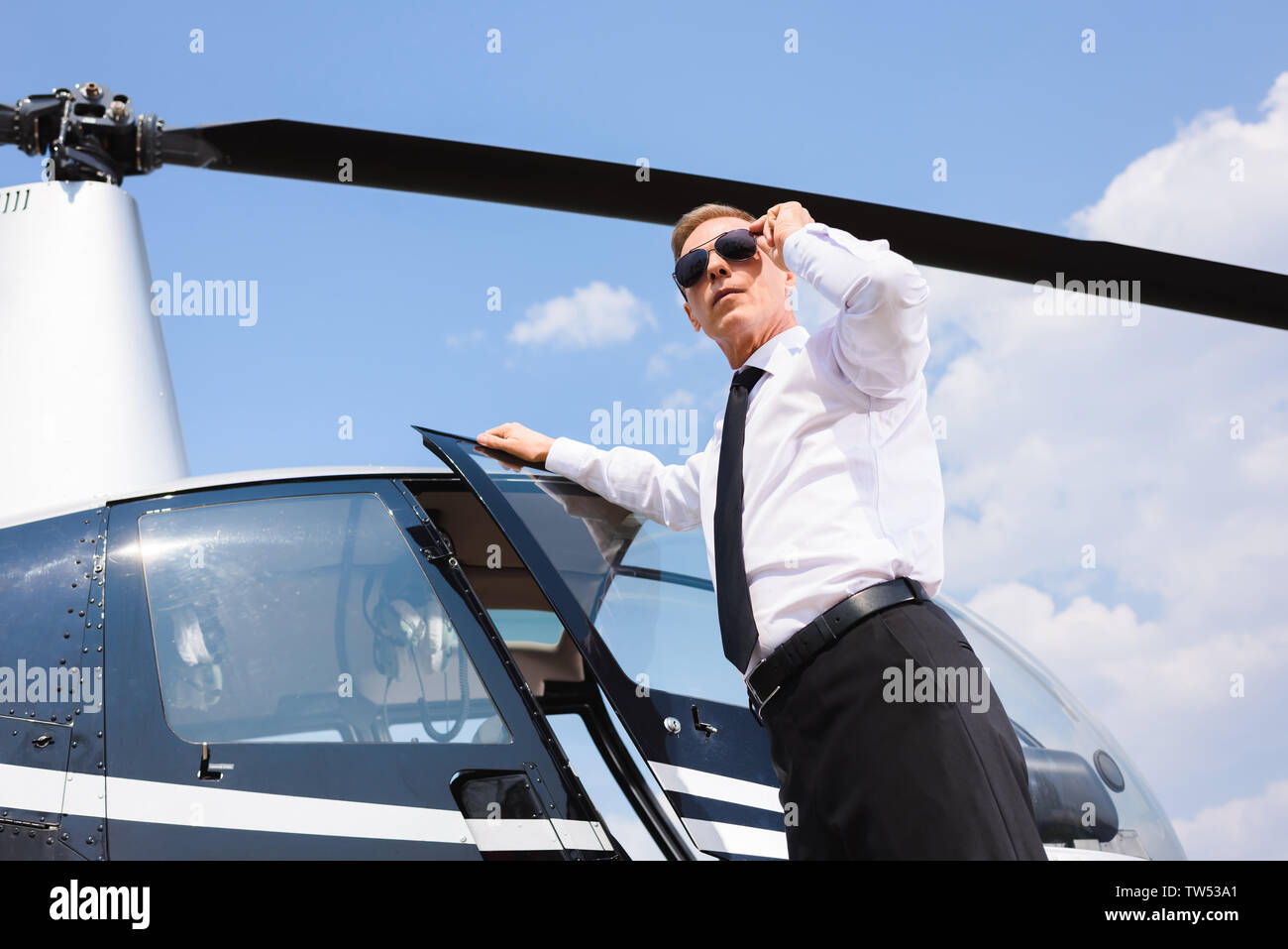 low angle view of Pilot in formal wear and sunglasses near helicopter ...