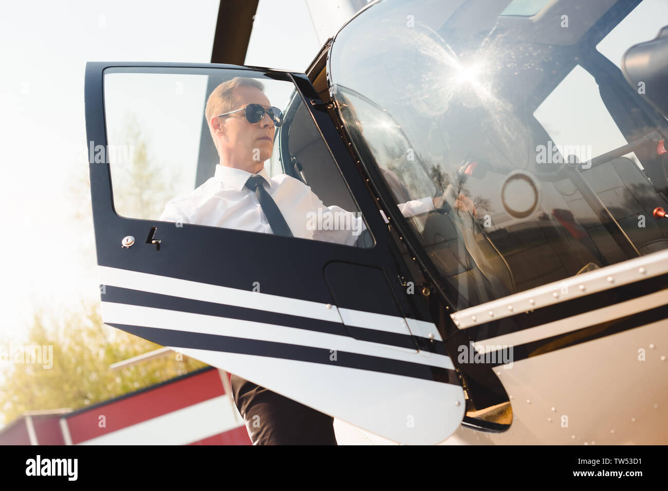 handsome Pilot in formal wear and sunglasses opening door of helicopter ...