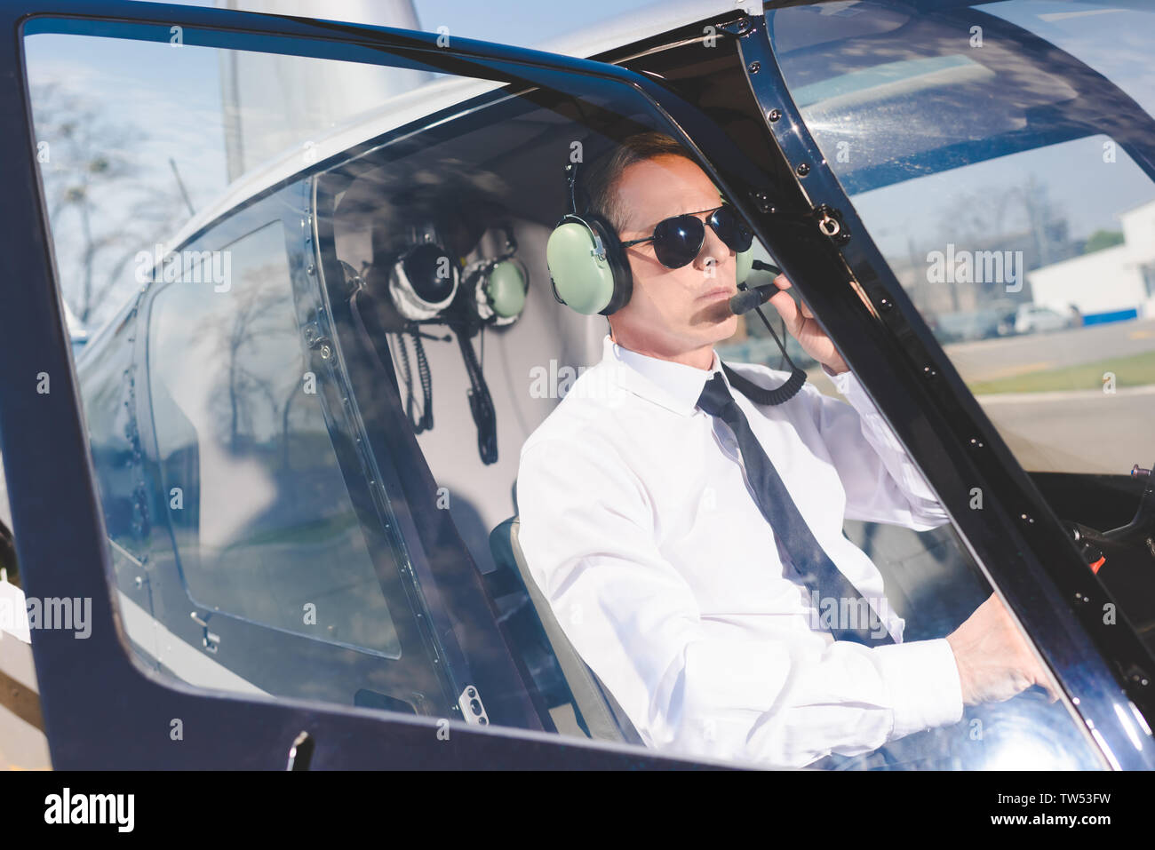 handsome mature Pilot in sunglasses and headset sitting in helicopter ...