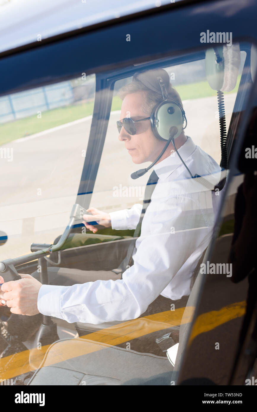 mature Pilot in sunglasses and headphones with microphone sitting in ...