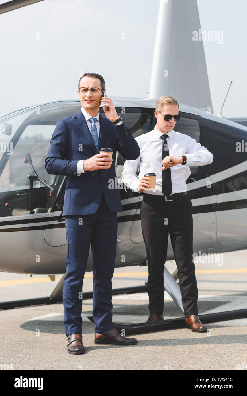 businessman with coffee to go talking on smartphone while pilot looking ...