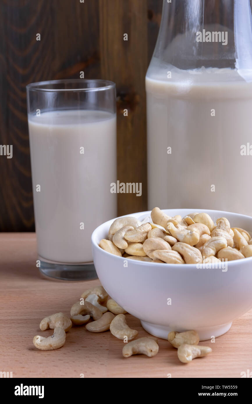 Glass of Cashew milk and bottle and organic cashew on wooden background ...