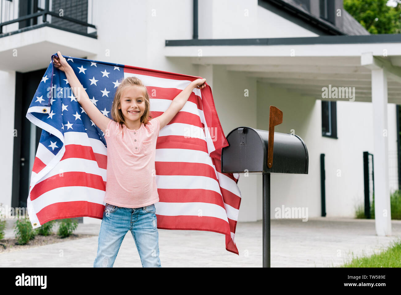 happy kid standing and holding american flag near mail box and house ...