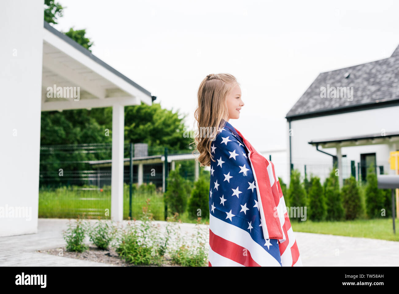 side view of happy kid smiling while standing with american flag near ...