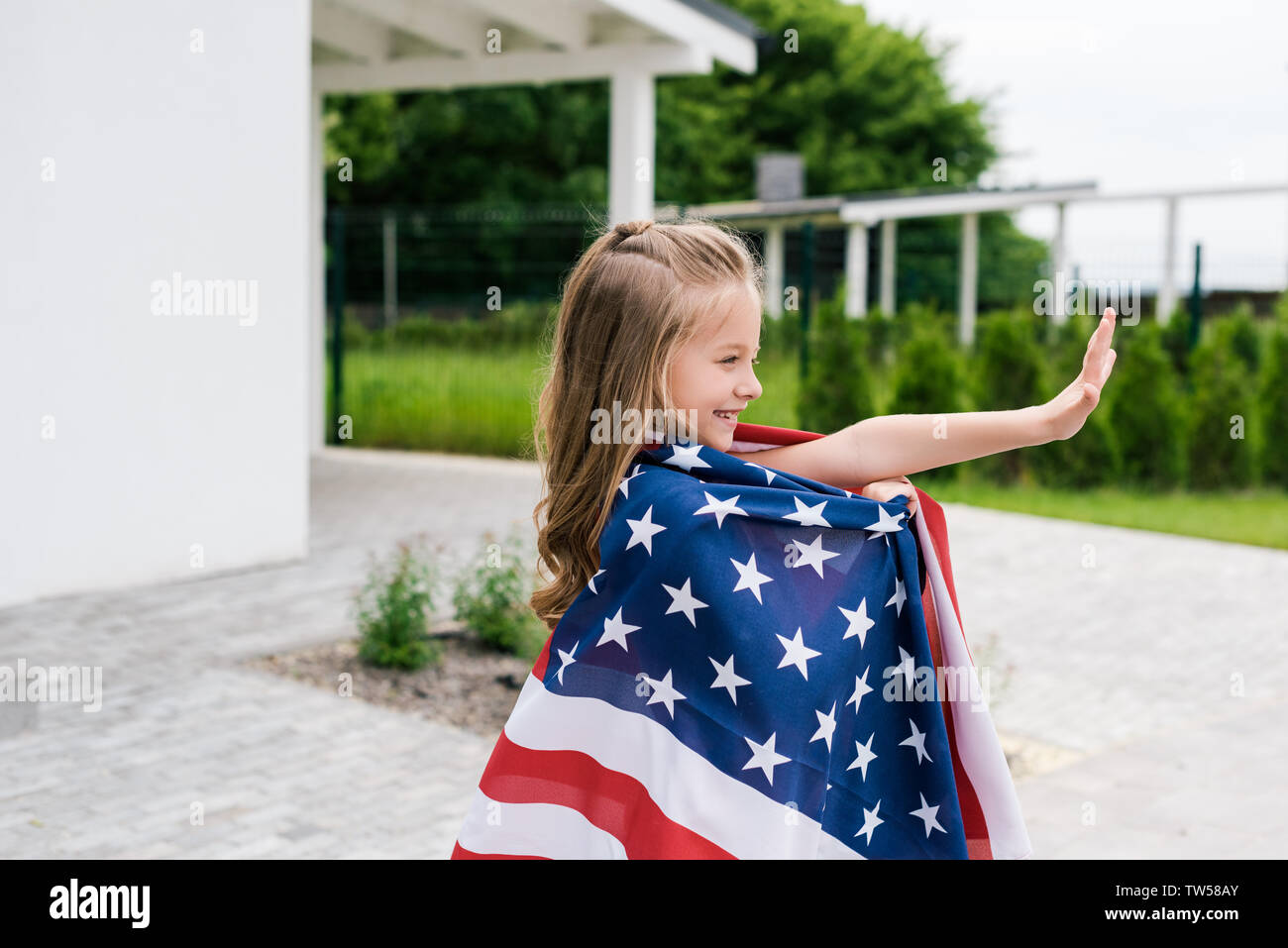 happy kid waving hand while standing with american flag near house ...