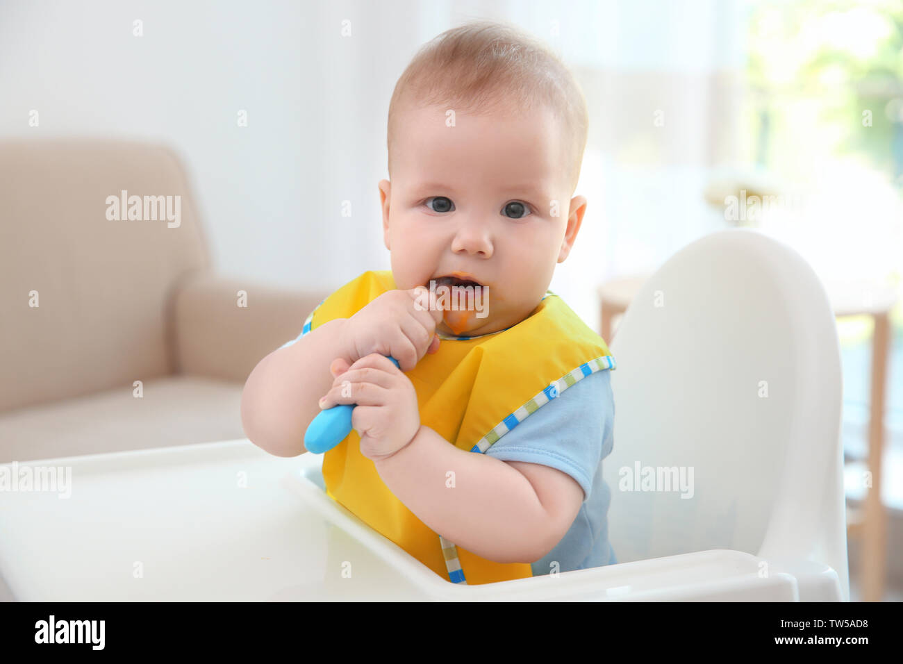 Cute baby with spoon sitting in kitchen Stock Photo - Alamy