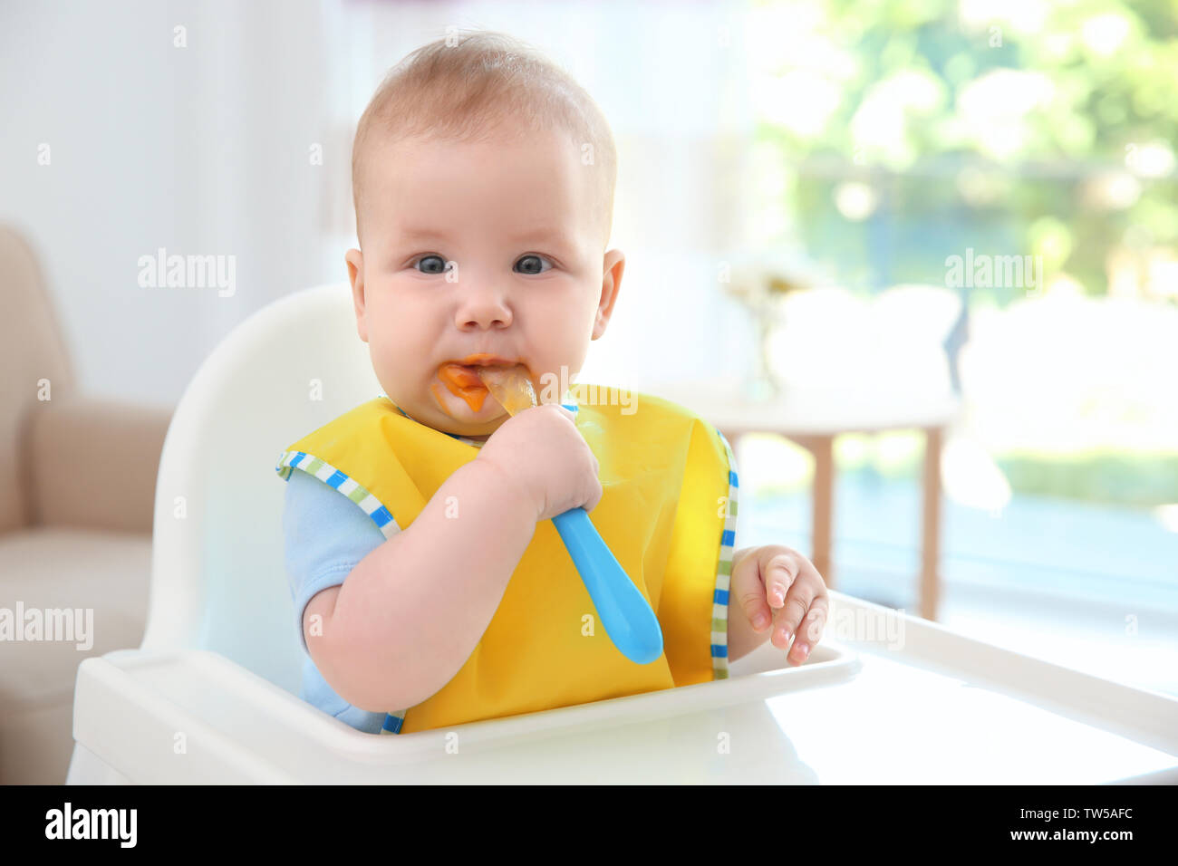 Cute baby with spoon sitting in kitchen Stock Photo - Alamy